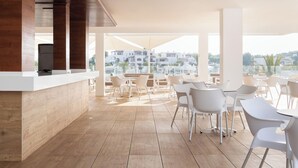 Uma área de estar ao ar livre moderna, com piso de madeira e cadeiras brancas, com vista para uma área residencial.