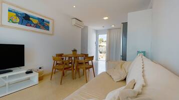 Uma sala de estar com televisão, mesa de jantar de madeira, cadeiras, sofá e um quadro na parede.