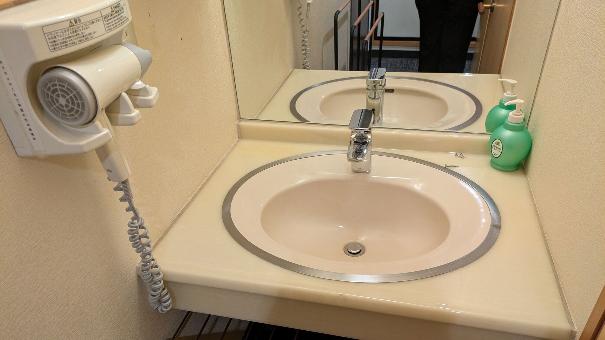 Casa de banho com lavatório, espelho, secador de cabelo e dispensador de sabonete.