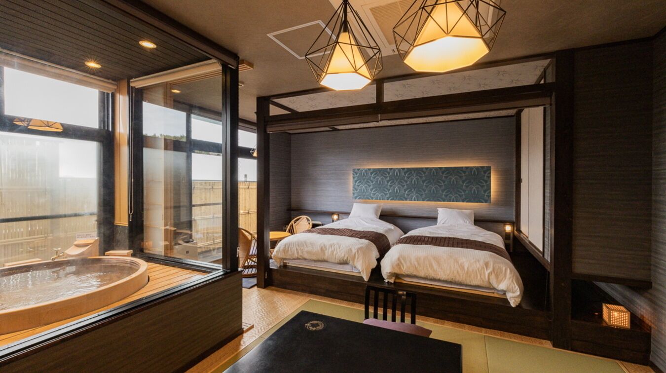 Quarto de hotel moderno com uma janela grande, uma banheira, duas camas e piso de madeira.