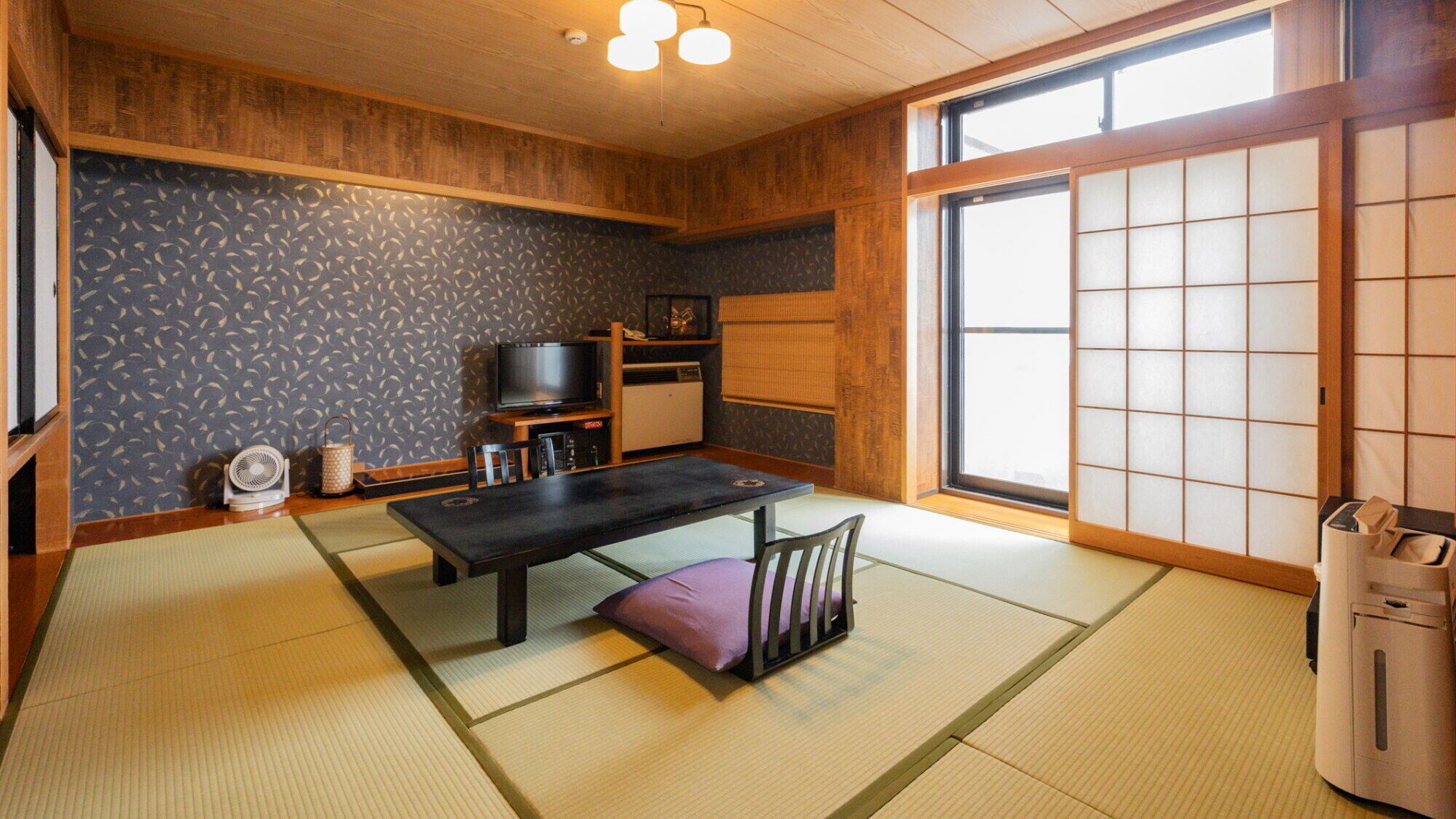 Um quarto japonês tradicional com tatames, uma mesa baixa, uma televisão e uma porta deslizante.