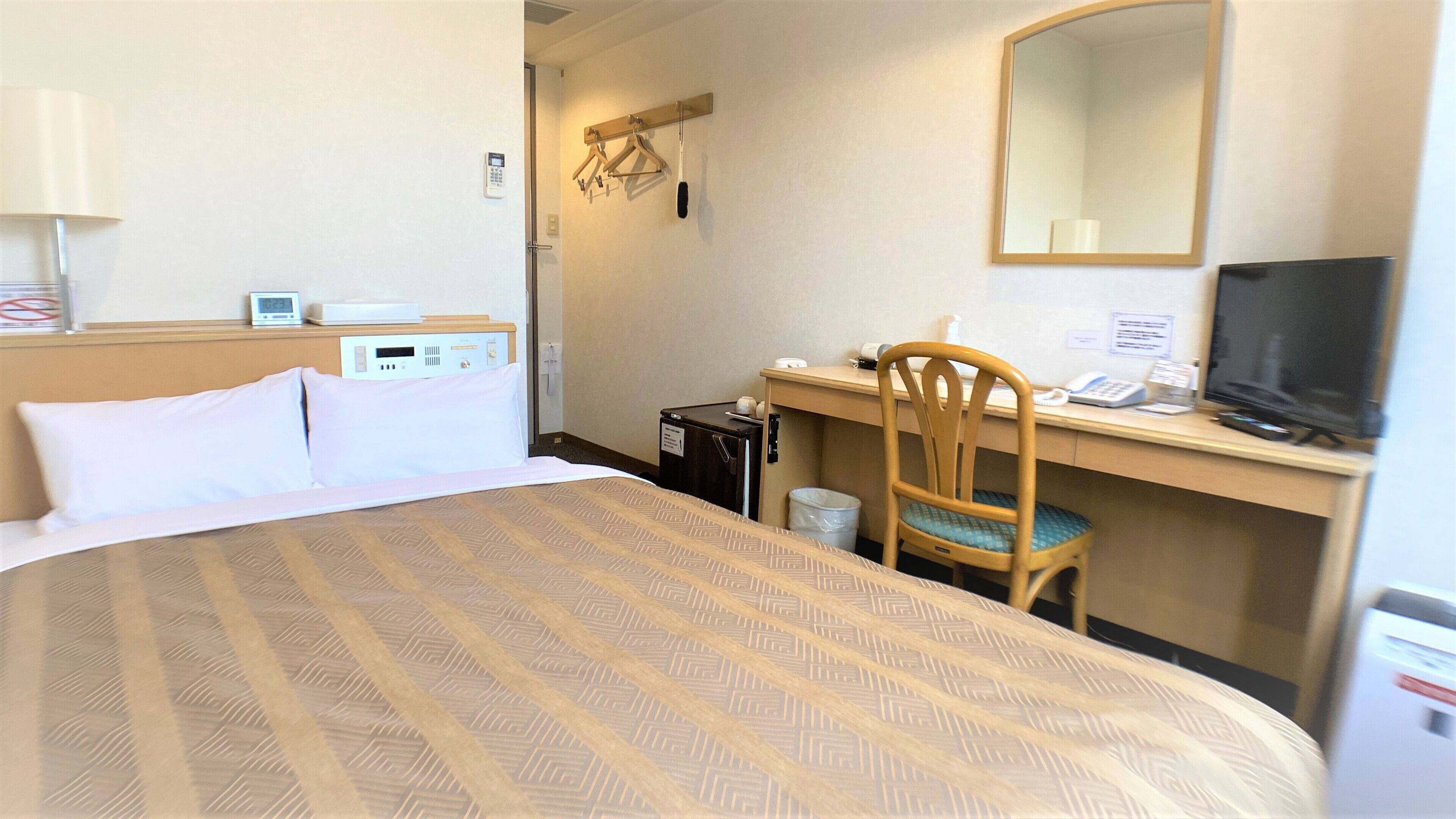 Quarto de hotel com cama, escrivaninha com computador e telefone, poltrona e televisão.