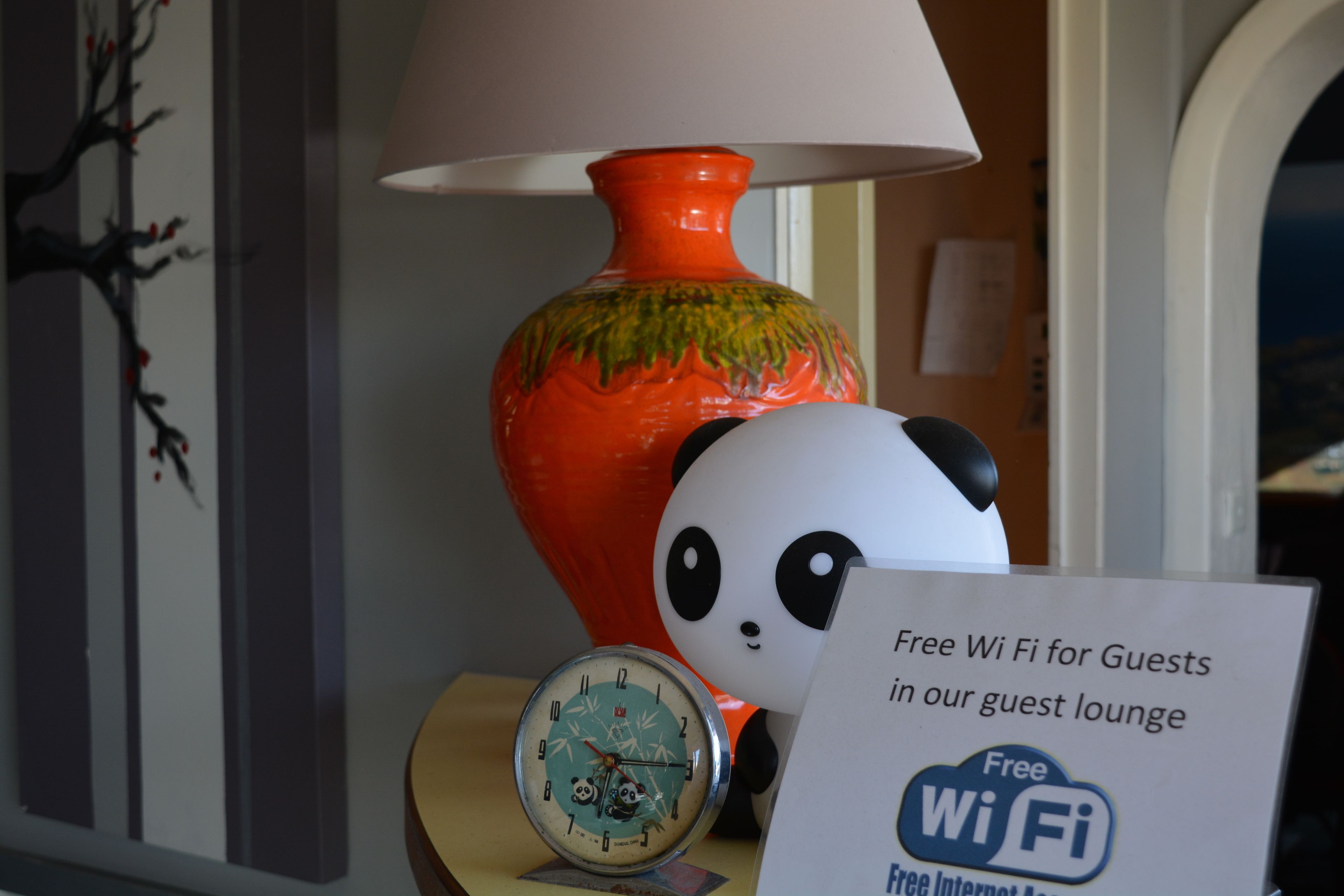 Um relógio, uma luminária, uma figura de panda e uma placa oferecendo WiFi gratuito na sala de hóspedes.