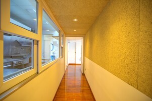 Um corredor com piso de madeira, um compartimento de vidro à esquerda e uma parede texturizada à direita.