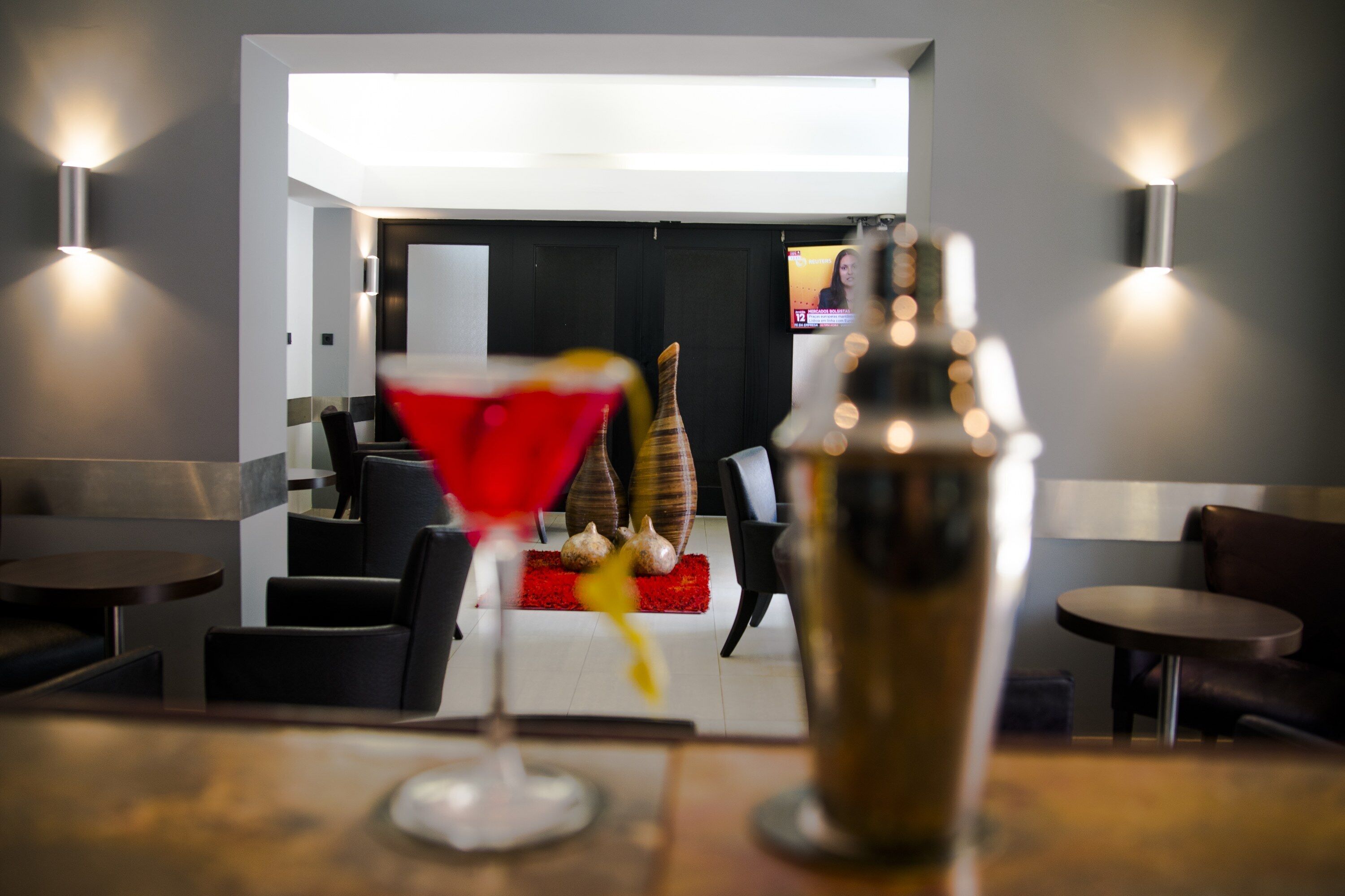 Uma área de bar com uma taça de martini e um coqueteleira, com assentos e uma televisão ao fundo.