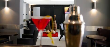 Uma área de bar com uma taça de martini e um coqueteleira, com assentos e uma televisão ao fundo.