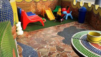 Uma área de recreação infantil com um escorrega, cadeiras pequenas e um cavalo de brinquedo.
