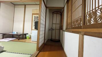 Quarto japonês tradicional com tatames, uma mesa de madeira baixa, uma geladeira branca e um futum com detalhes ornamentais.