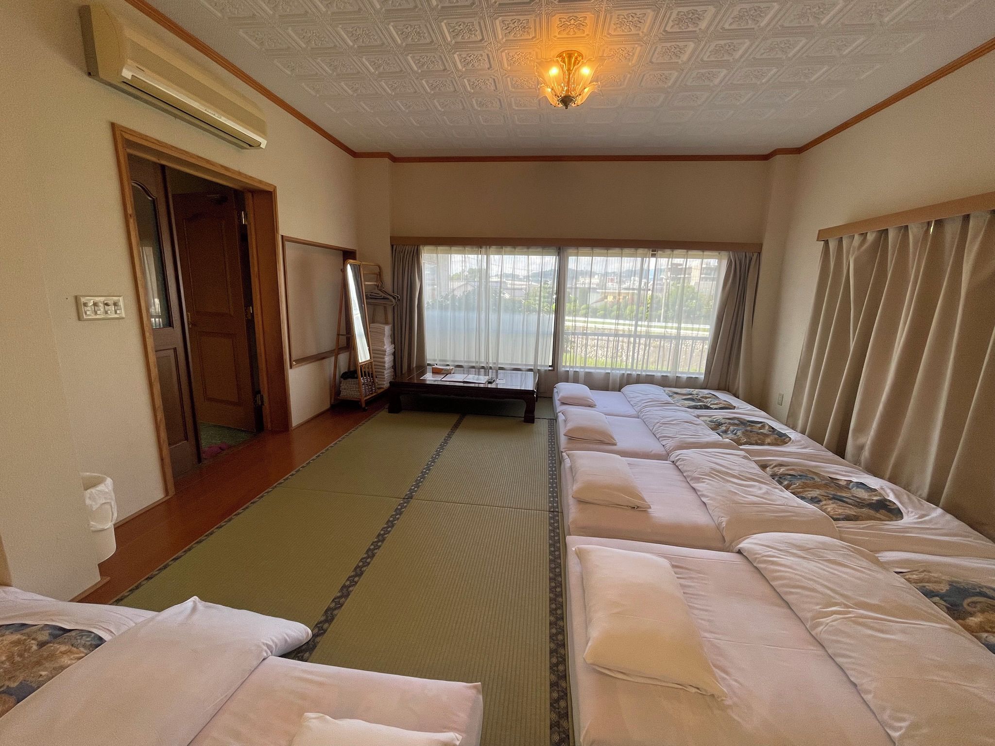 Quarto de hotel com uma cama grande, um espelho, uma janela com cortinas e um teto com padrão decorativo.