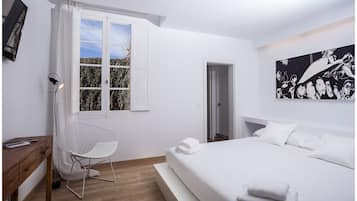 Um quarto com uma cama grande, uma cadeira, uma escrivaninha e uma janela.