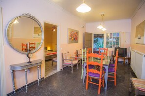 Uma sala de jantar com um espelho redondo, uma mesa com cadeiras e uma televisão.