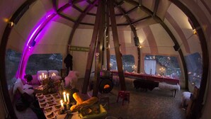 Interior acolhedor de iglu, com lareira central, mesas preparadas para refeições e vista para o exterior.