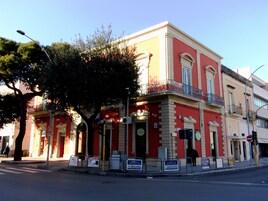 Um edifício vermelho com varanda, uma árvore na frente e uma placa de 'Não Estacionar'.