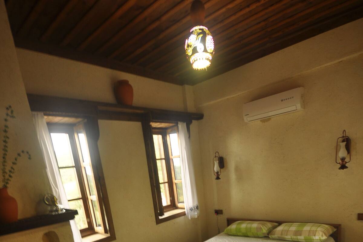 Quarto com teto de madeira, cama com roupa de cama branca, tapete colorido e lareira.