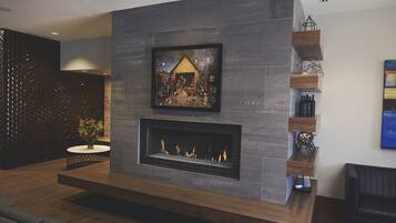 Uma sala de estar moderna com lareira, um quadro emoldurado acima dela e uma estante de madeira com objetos decorativos.