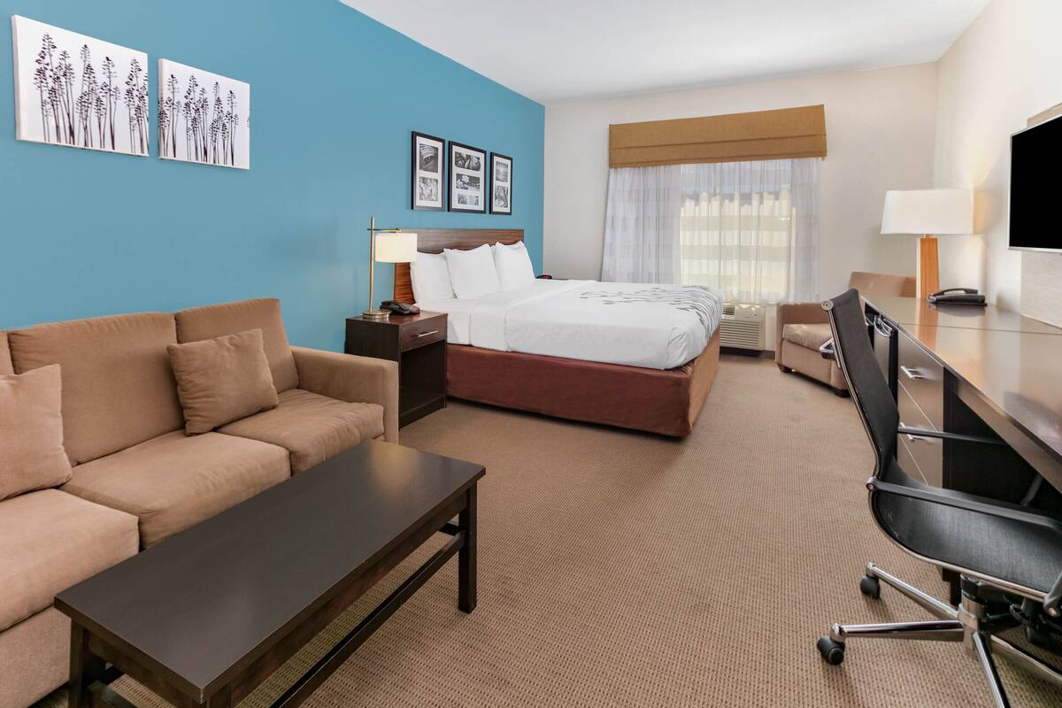 Quarto de hotel com cama, sofá, escrivaninha, cadeira e televisão.