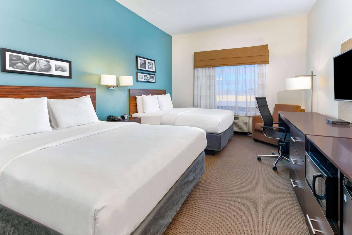 Quarto de hotel com duas camas, uma mesa, uma cadeira, televisão e janela com cortinas.