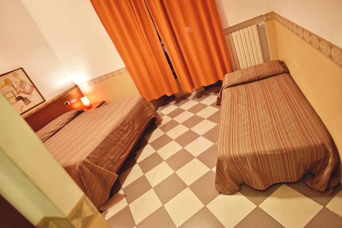 Quarto com duas camas, piso xadrez e cortinas laranja.