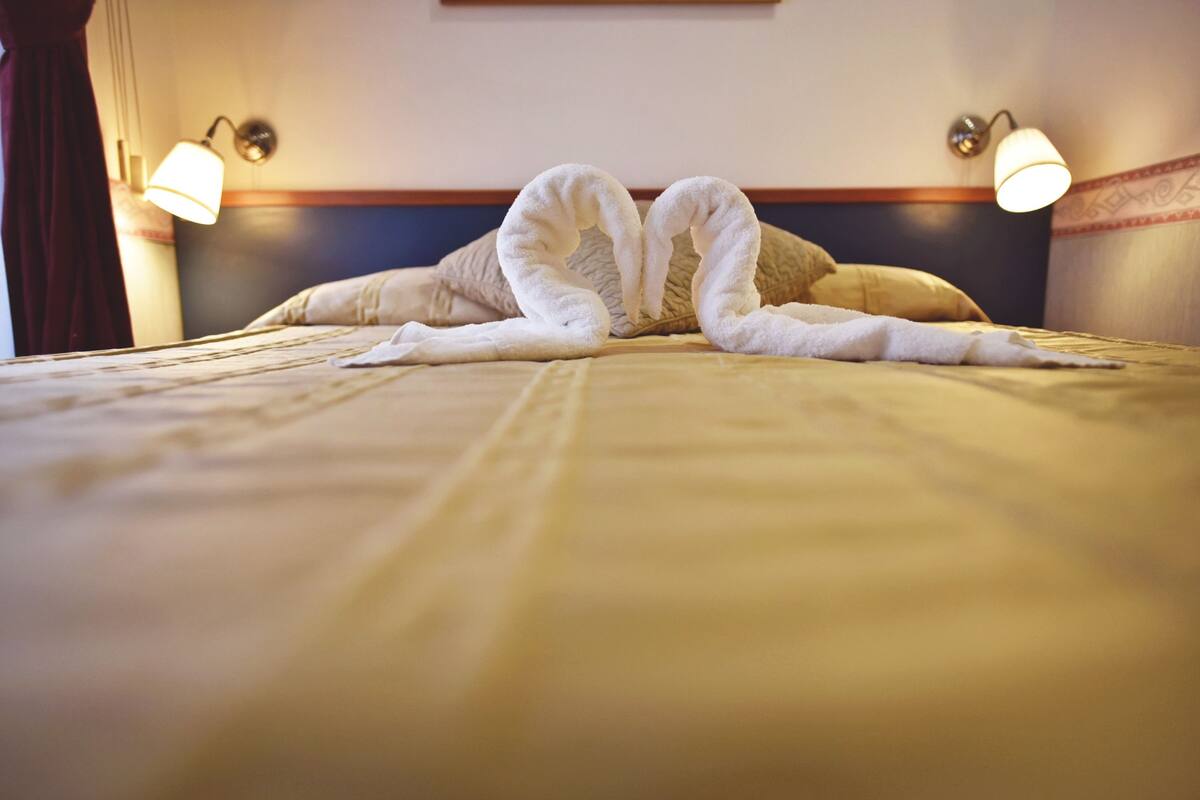 Cama com arranjo de toalhas em formato de coração e duas luminárias de parede.