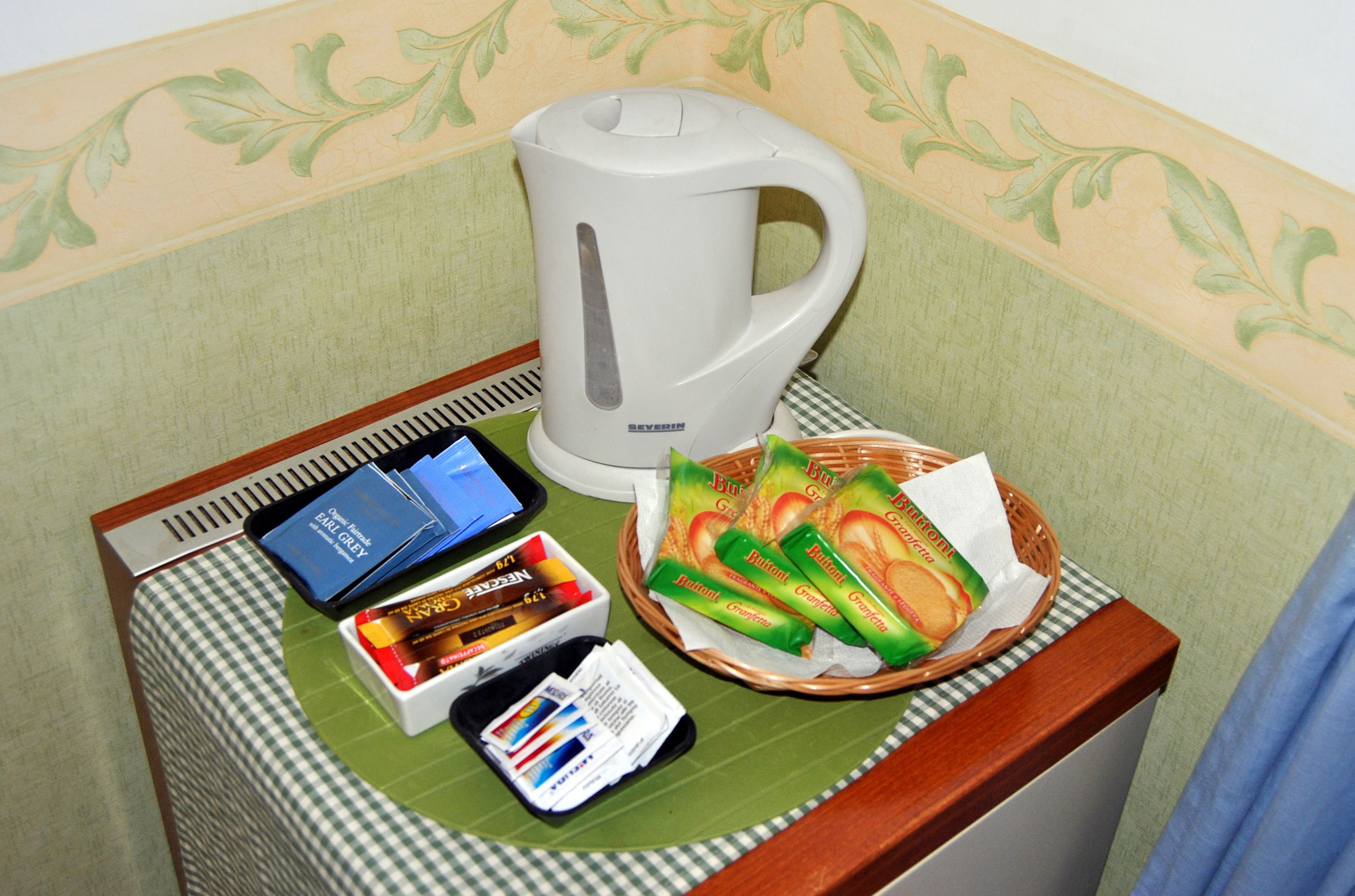 Uma bandeja com chaleira, um smartphone, caixa de lenços e cesta de lanches sobre toalha xadrez.