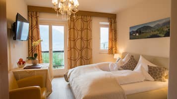 Quarto de hotel com cama, televisão, mesa de jantar com cadeiras, janela com cortinas e um quadro na parede.