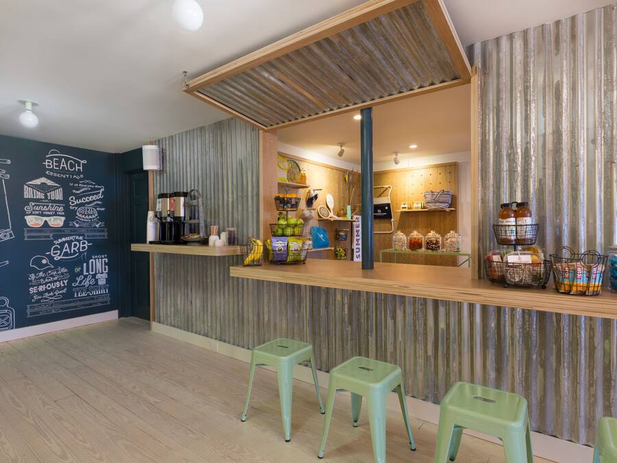 Uma área de bar moderna com balcão de madeira, banquetas verdes e uma parede com frases motivacionais.