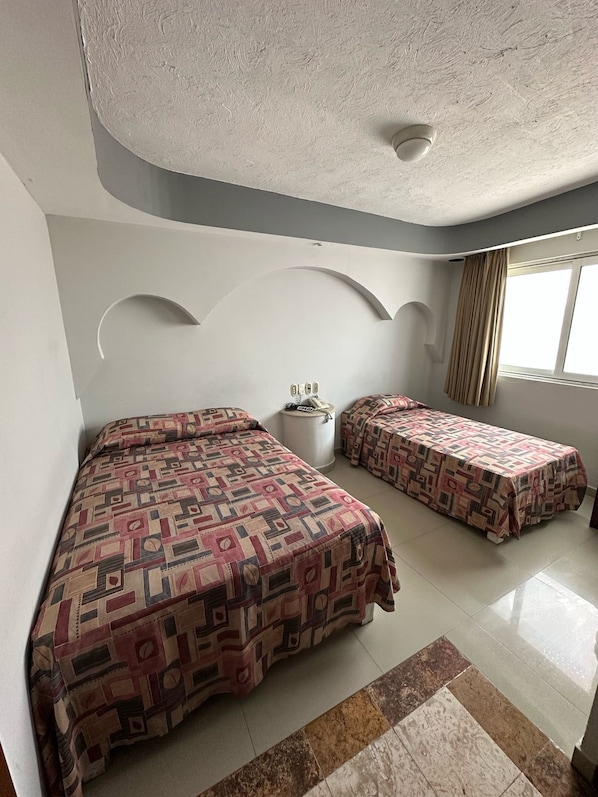 Quarto com duas camas, uma mesinha e uma janela com cortinas.