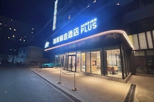 Entrada de hotel com fachada de vidro, placa de identificação e um carro azul estacionado.