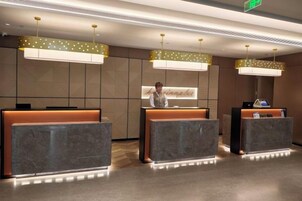 Área de recepção de hotel, com três balcões, um recepcionista e um balcão de atendimento.