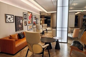 Um saguão de hotel moderno com sofá, cadeiras, mesas e obras de arte nas paredes.