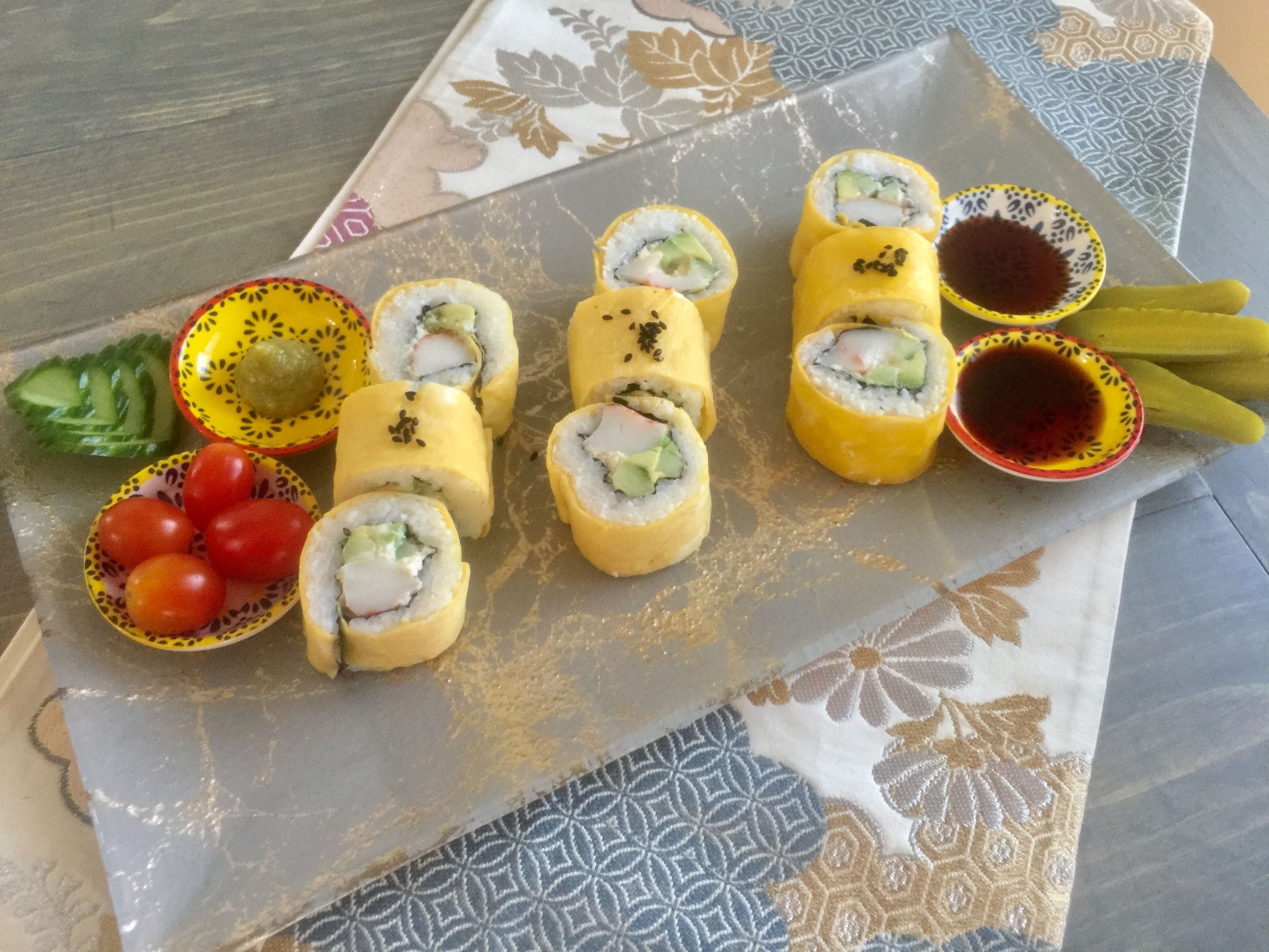 Uma mesa com sushi, tomate cereja, vegetais em conserva e molho de soja.