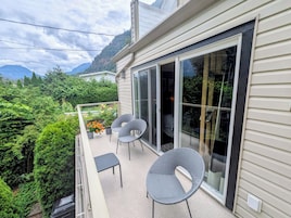 Varanda com duas cadeiras e uma mesa, com vista para um jardim exuberante e montanhas.