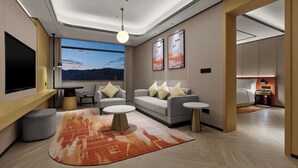 Uma sala de estar moderna com uma TV grande, assentos confortáveis, uma mesa de centro e vista para o exterior.