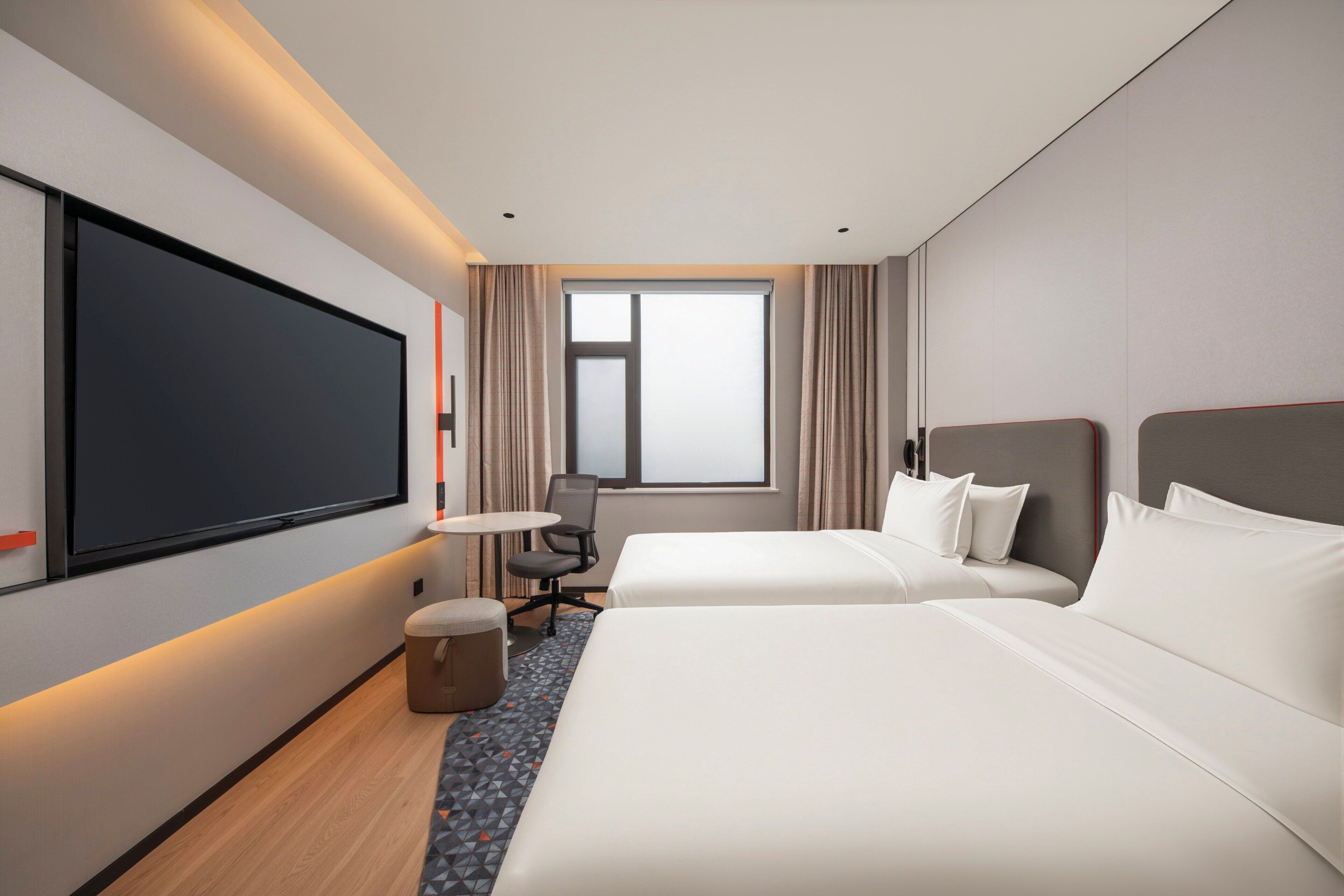 Quarto de hotel com duas camas, televisão, uma mesinha e janela com cortinas.