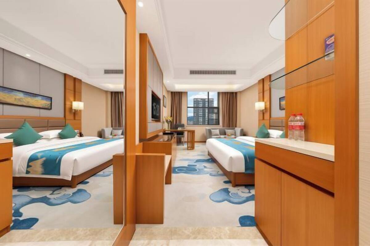 Quarto de hotel com duas camas, uma escrivaninha, uma cadeira e vista para a cidade.