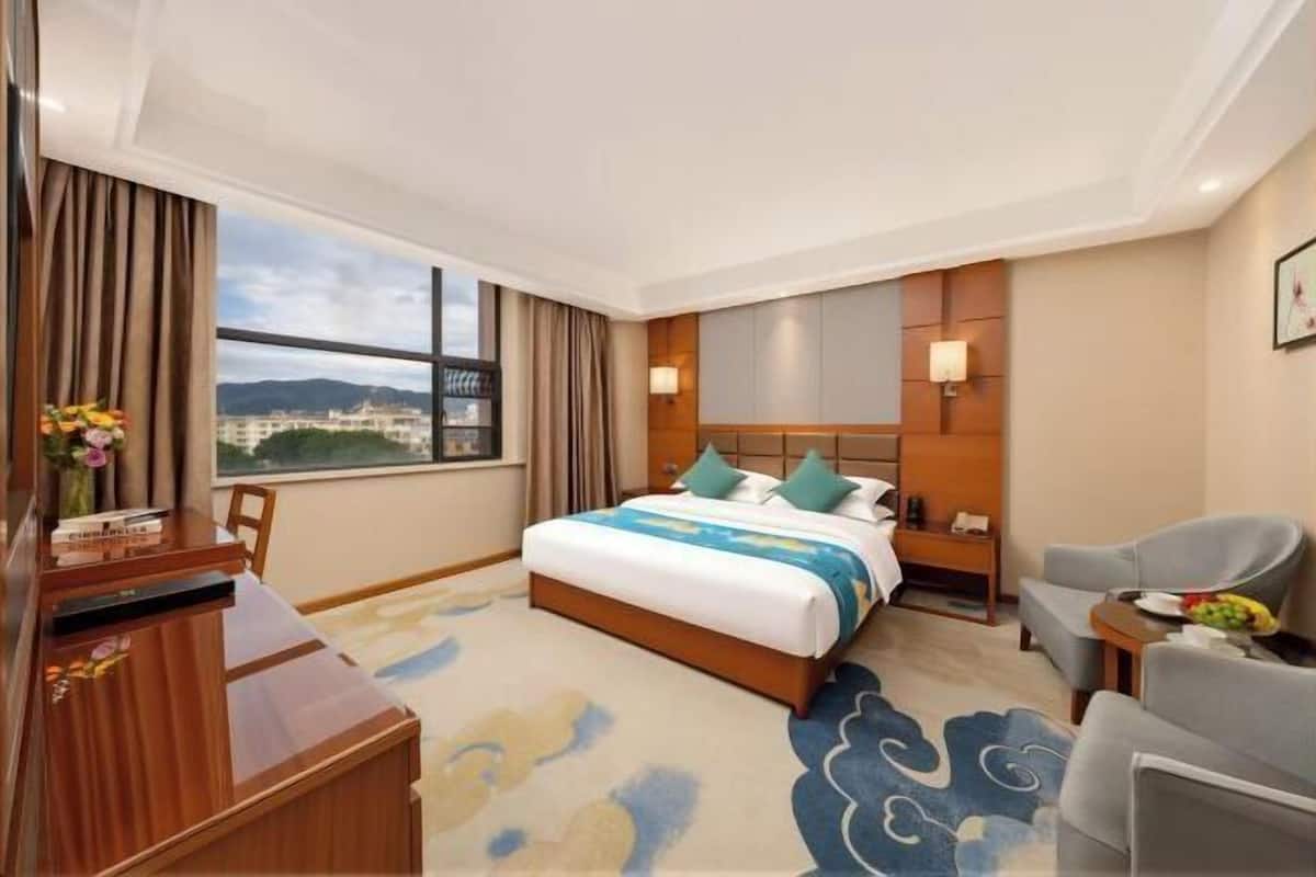 Quarto de hotel com cama, mesa, cadeira, mesa de cabeceira e vista para a cidade.