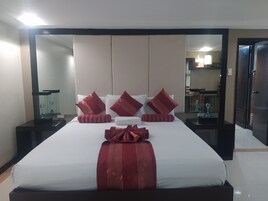Cama bem arrumada com roupa de cama branca e vermelha, um espelho grande em cima e uma porta de madeira à direita.