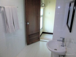 Casa de banho com uma sanita branca, uma porta de madeira e um porta-toalhas com duas toalhas.