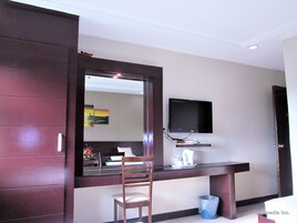 Quarto de hotel com secretária de madeira, cadeira, televisão fixada na parede e lixeira.