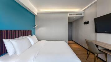 Quarto de hotel moderno com uma cama grande, uma escrivaninha e uma televisão.