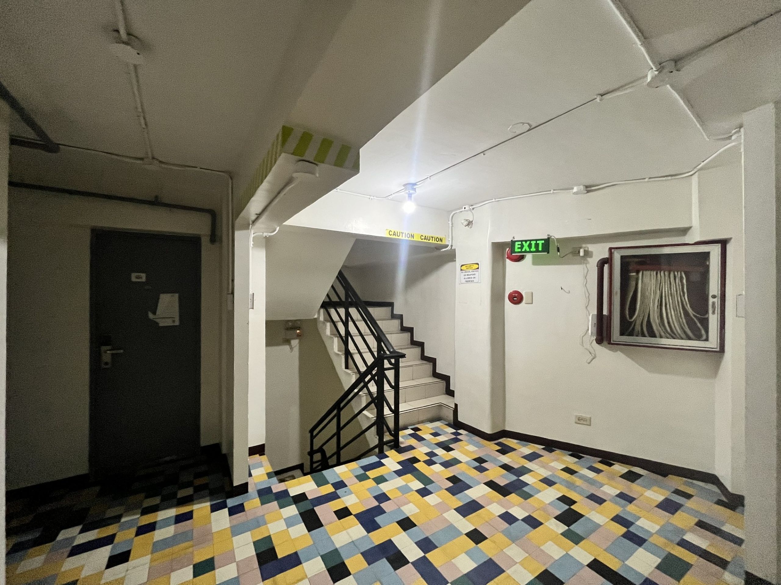 Um corredor com piso estampado, uma escada e um sinal de saída.