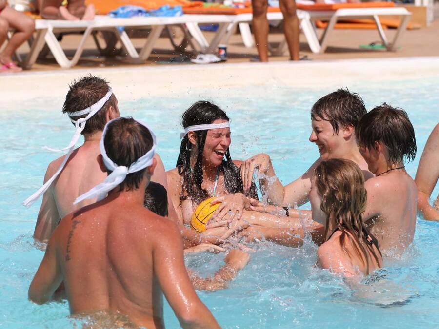 Um grupo de pessoas em uma piscina, algumas segurando uma bola amarela.