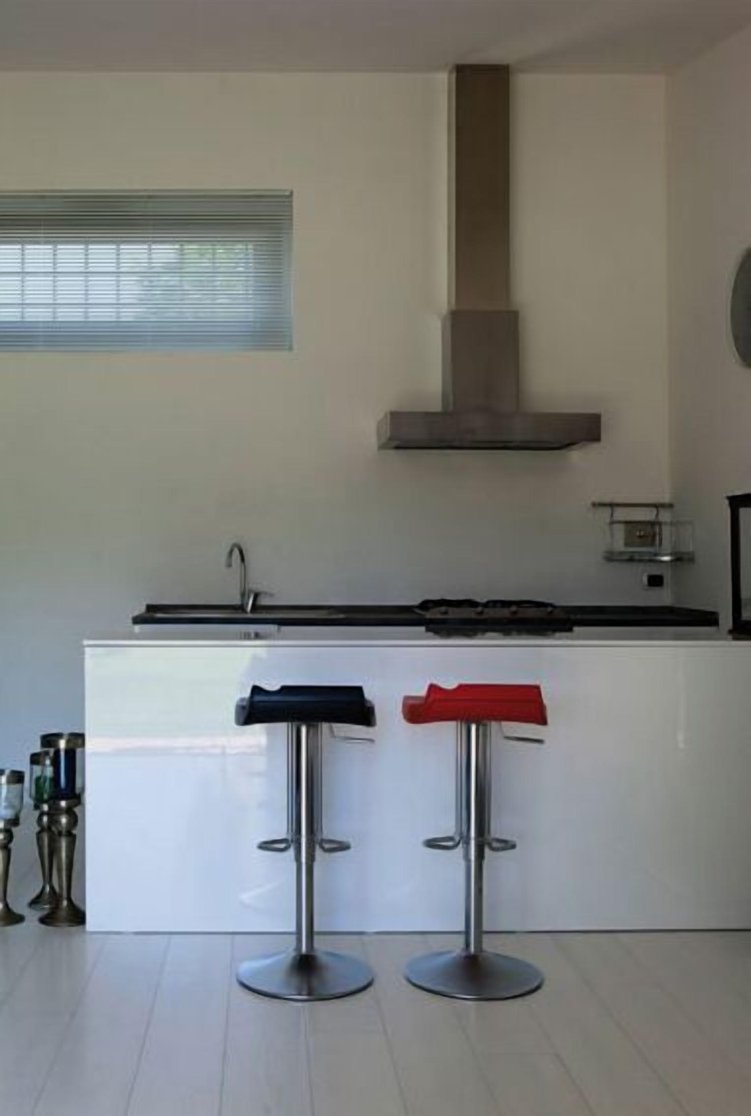 Uma cozinha moderna com uma ilha central, dois bancos altos, um exaustor de aço inoxidável e uma janela com persianas.