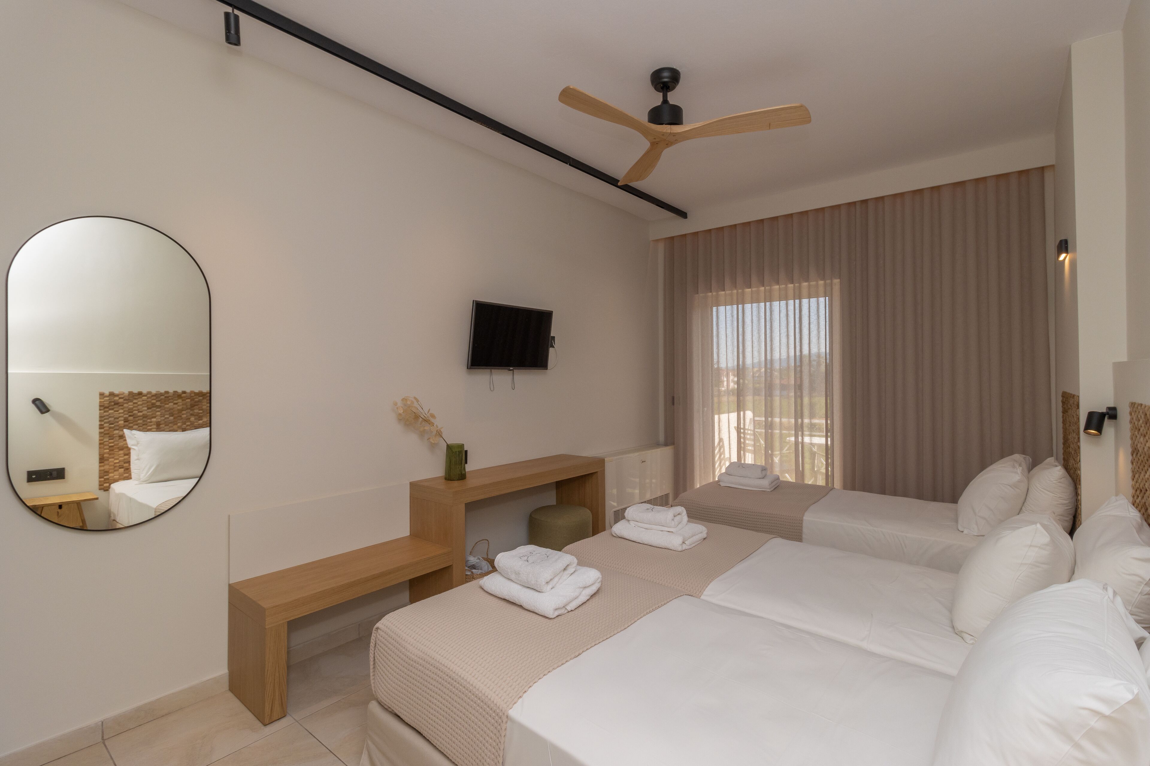 Quarto de hotel com uma cama grande, um banco de madeira, uma TV e um ventilador de teto.