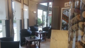 Um hall de hotel com balcão de recepção, várias cadeiras pretas, uma pequena mesa com plantas e uma escada ao fundo.