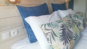 Uma cama com almofadas azuis e brancas, cabeceira de madeira e luminárias fixadas na parede.