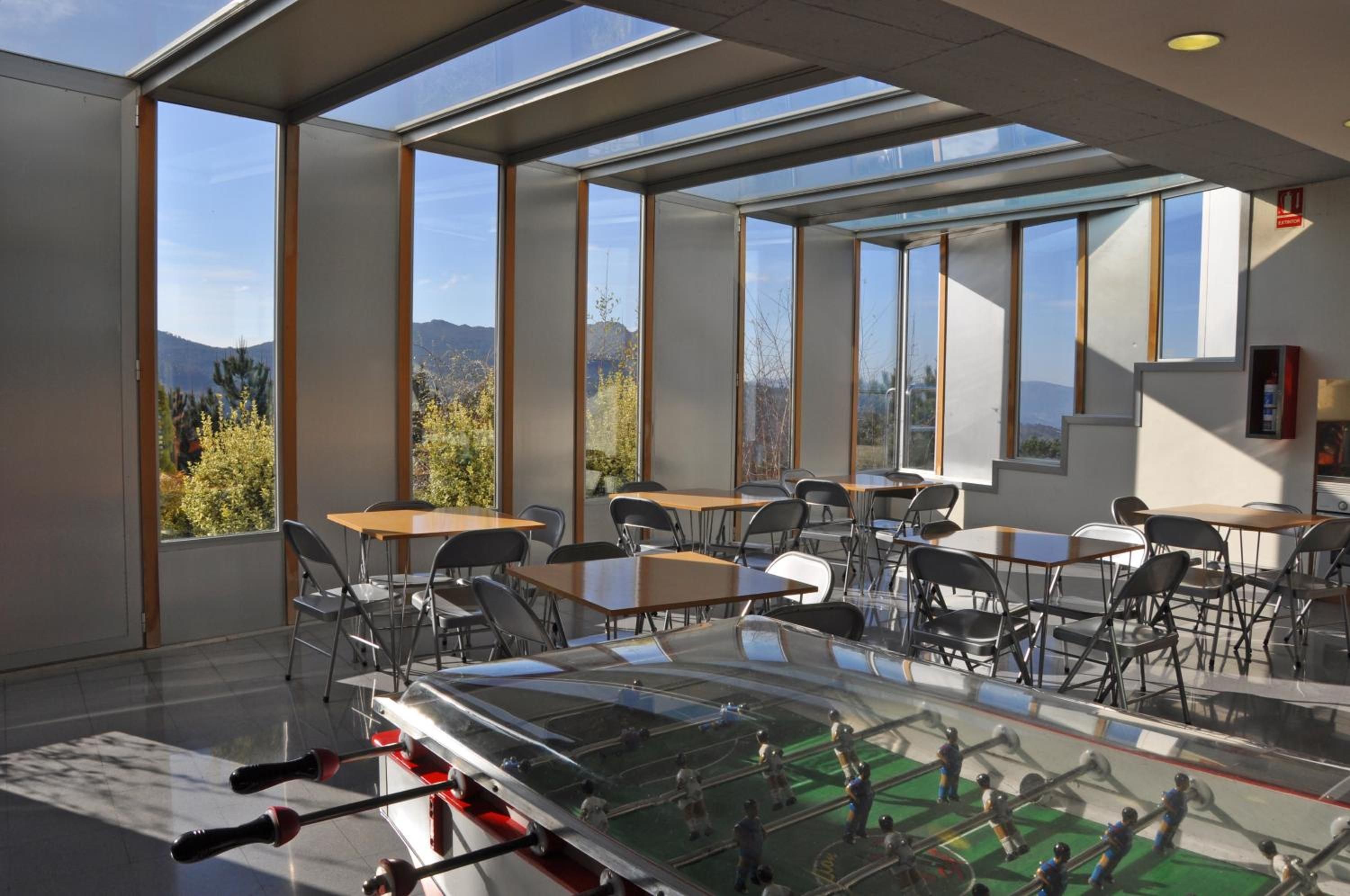 Um espaço interior moderno com amplas janelas, mesas, cadeiras e uma mesa de futebol.