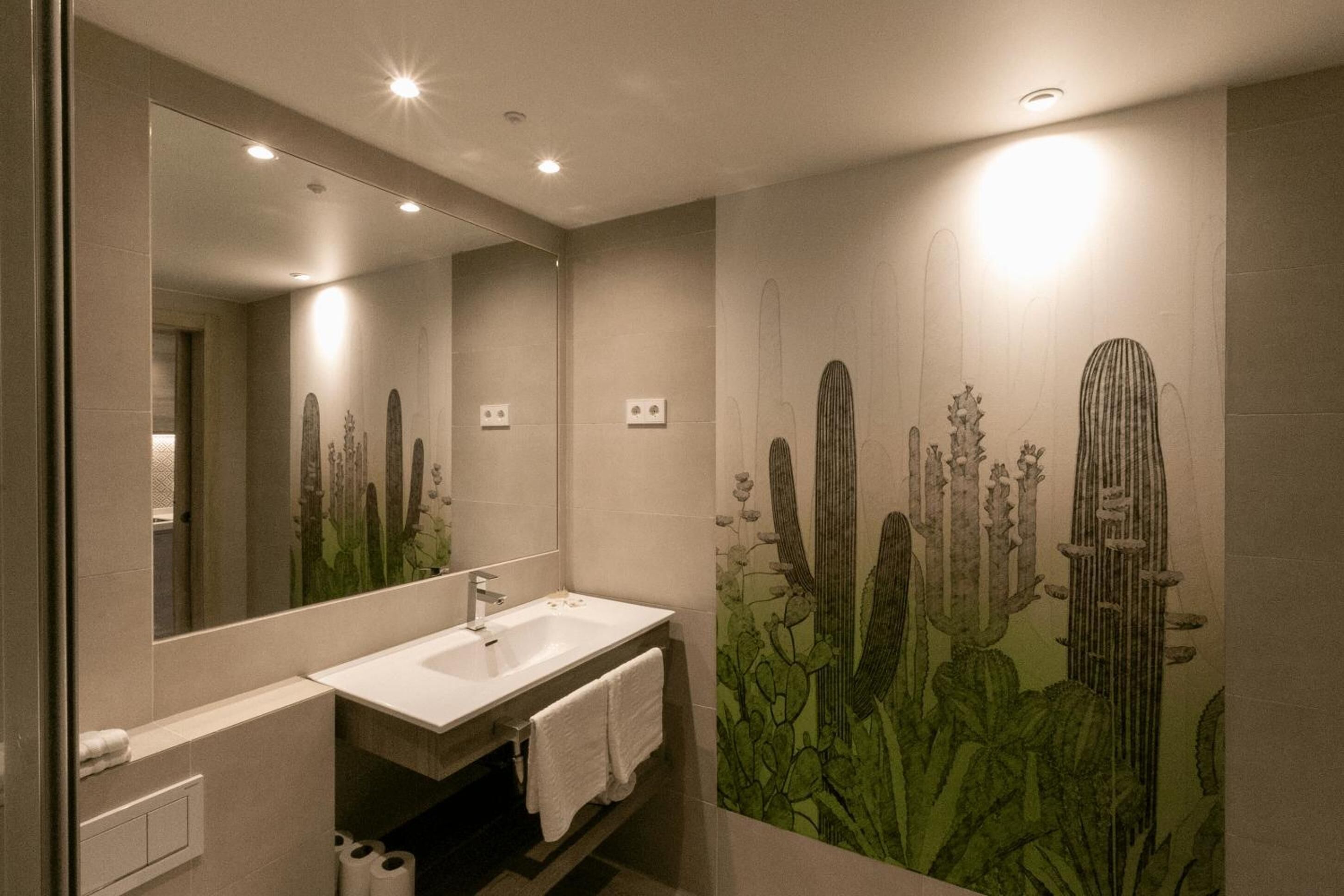 Casa de banho com lavatório, espelho e mural de cactos.