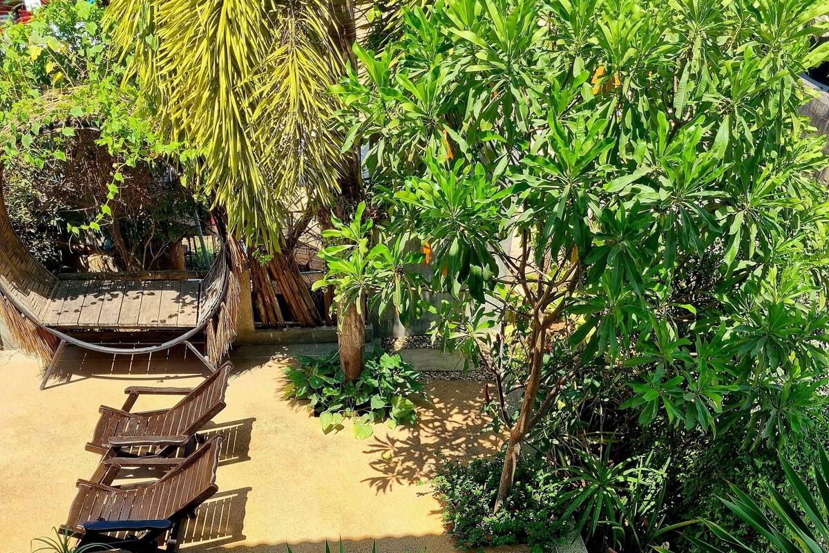 Uma área de jardim com uma rede, cadeiras de estar de madeira e uma escada com corrimão vermelho.