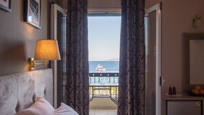 Quarto de hotel com cama, mesa de cabeceira, abajur e vista para o mar através de cortinas abertas.